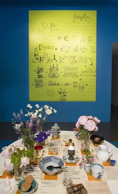 レイの典型的な庭で摘み取られた物や花を示す、判じ物とダイニングテーブルのクローズアップ。チャールズの娘ルシアの詩が活字でテーブルの表面に現れます。
